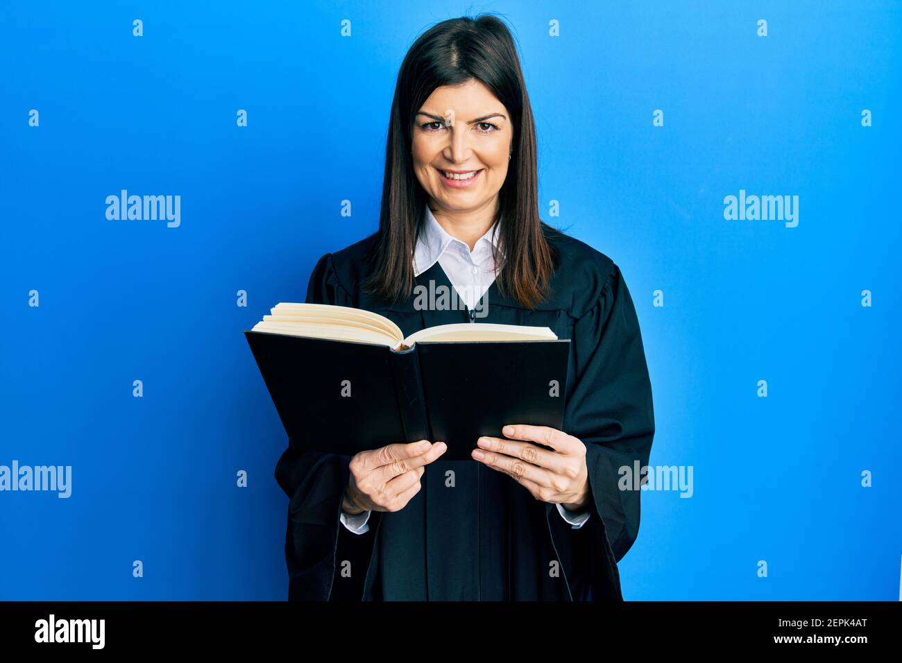 Young hispanic woman wearing judge uniform reading book looking ...