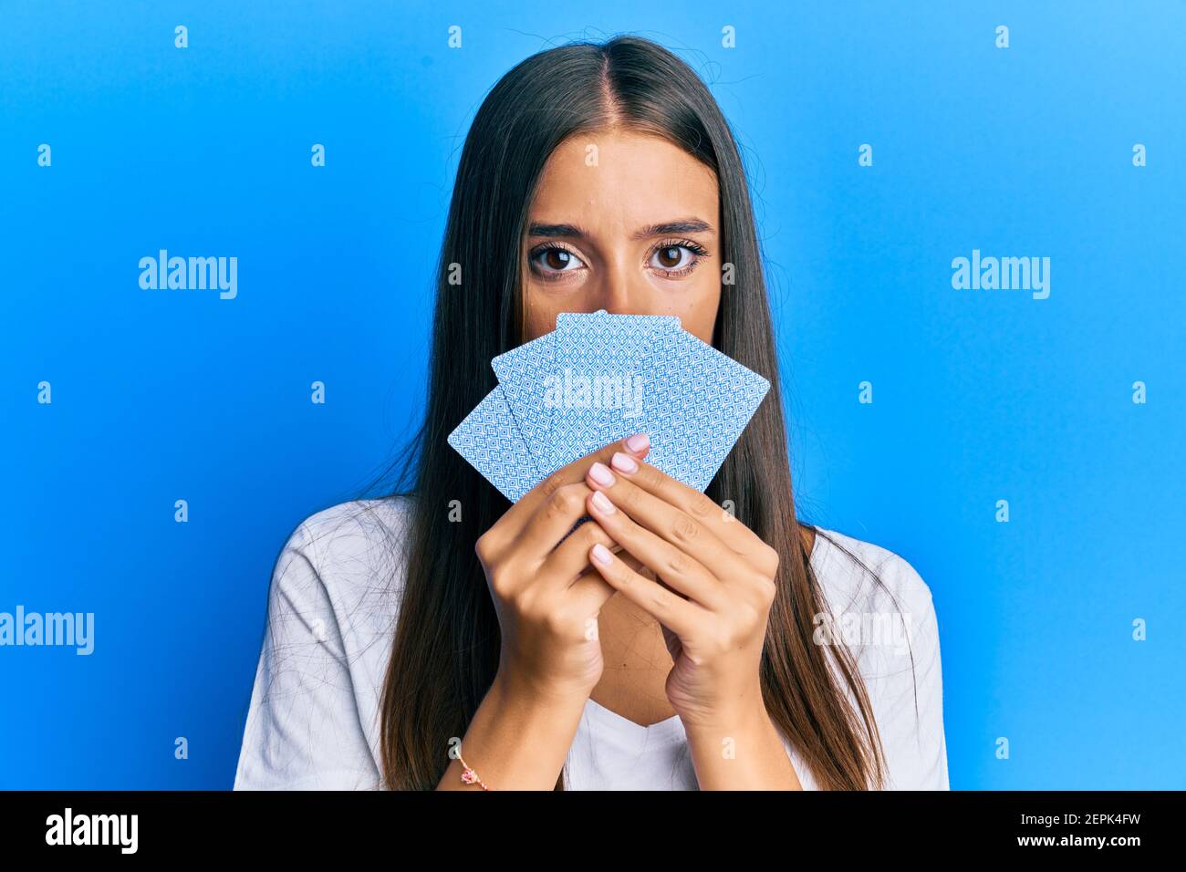 Young hispanic woman playing gambling poker covering face with cards ...