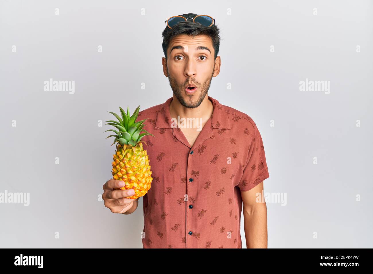 Young handsome man holding pineapple scared and amazed with open mouth ...
