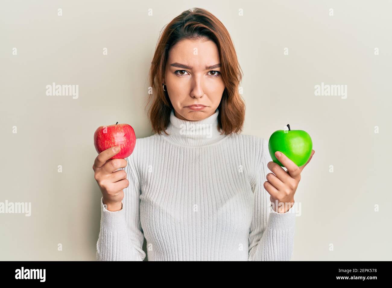 Young caucasian woman holding red and green apple depressed and worry ...