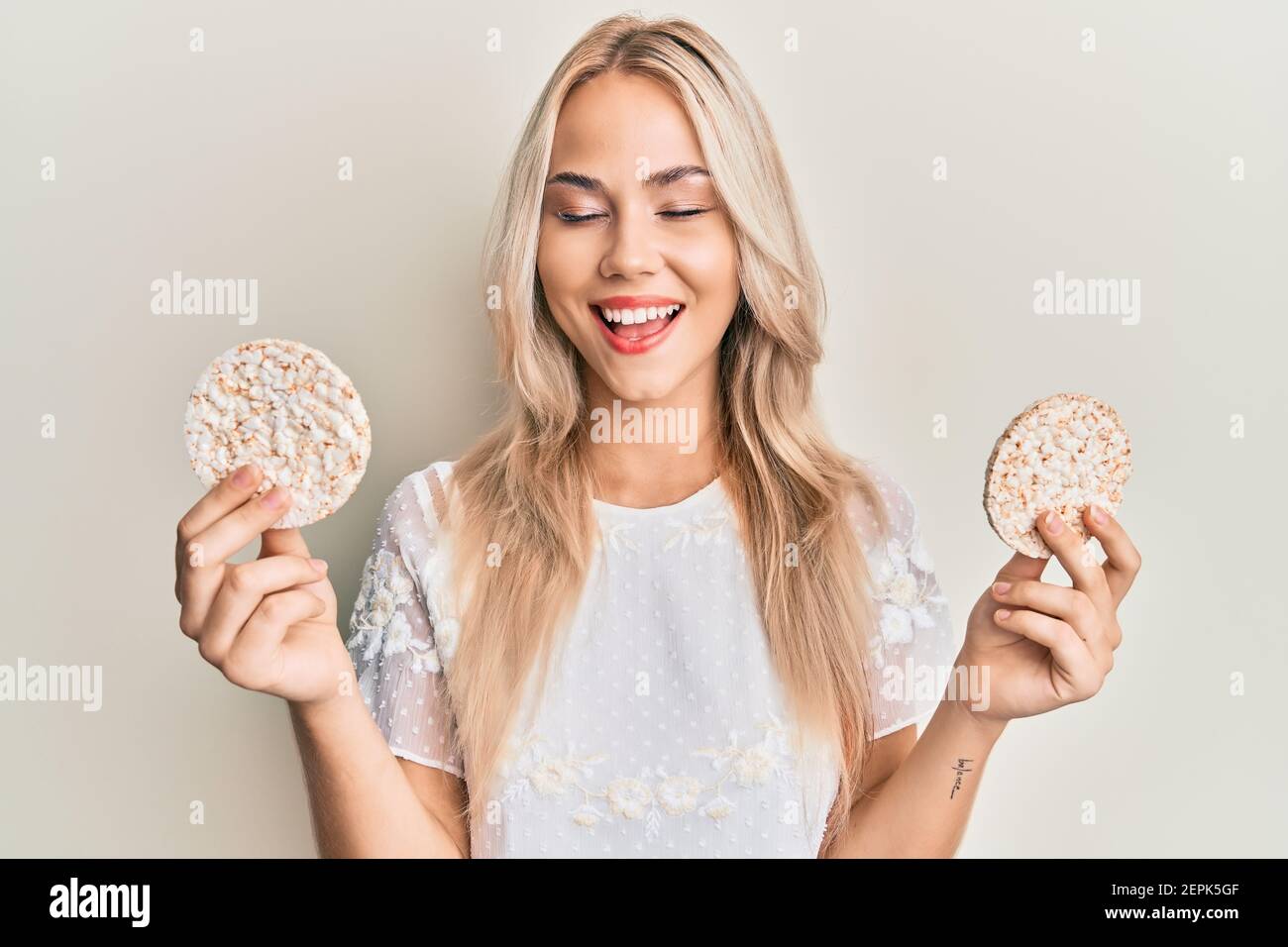 Beautiful caucasian blonde girl eating healthy rice crackers smiling ...