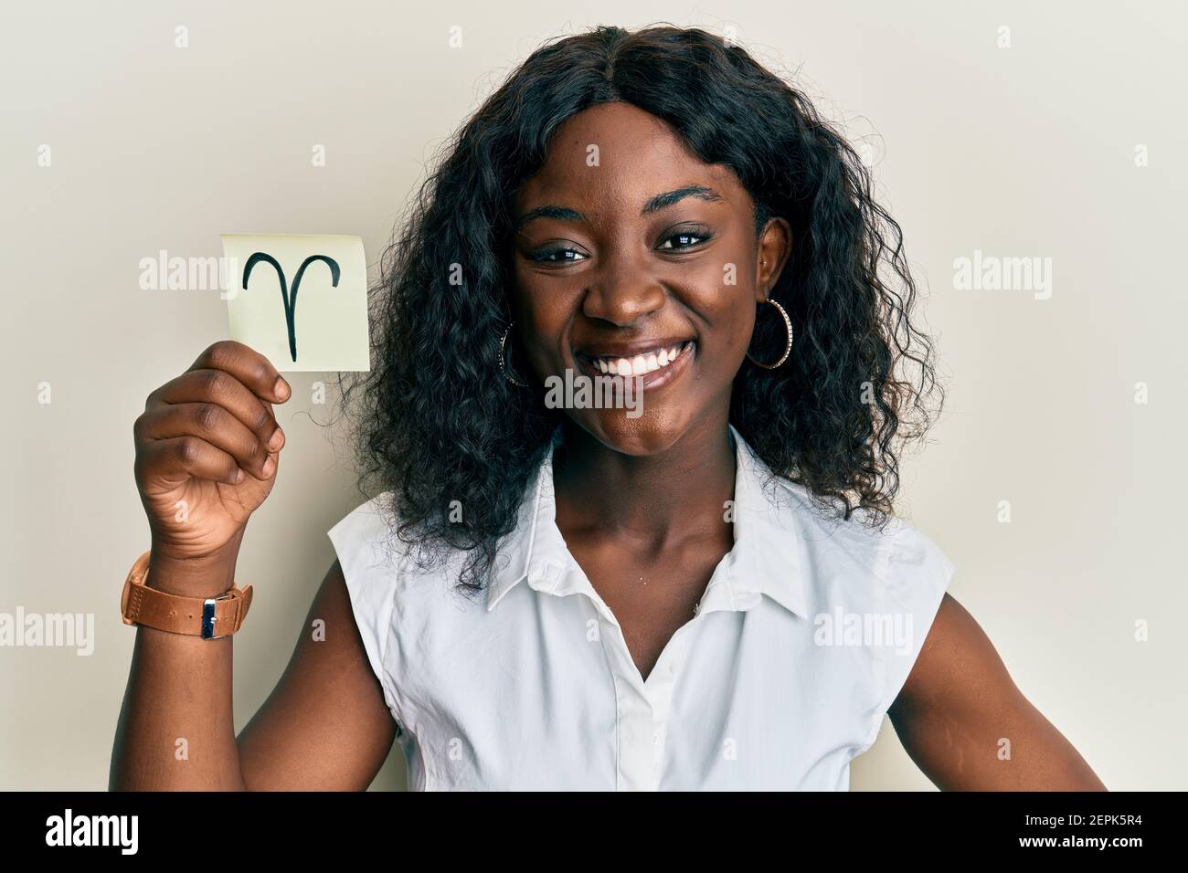 Beautiful african young woman holding paper with aries zodiac sign ...