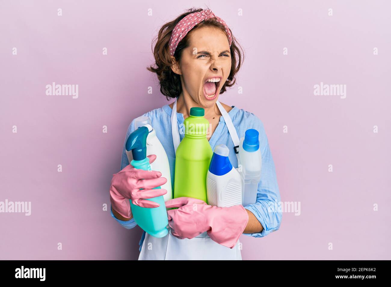 Young brunette woman wearing cleaner apron holding cleaning products ...