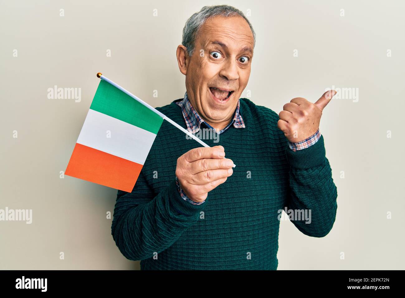 Handsome senior man with grey hair holding ireland flag pointing thumb ...