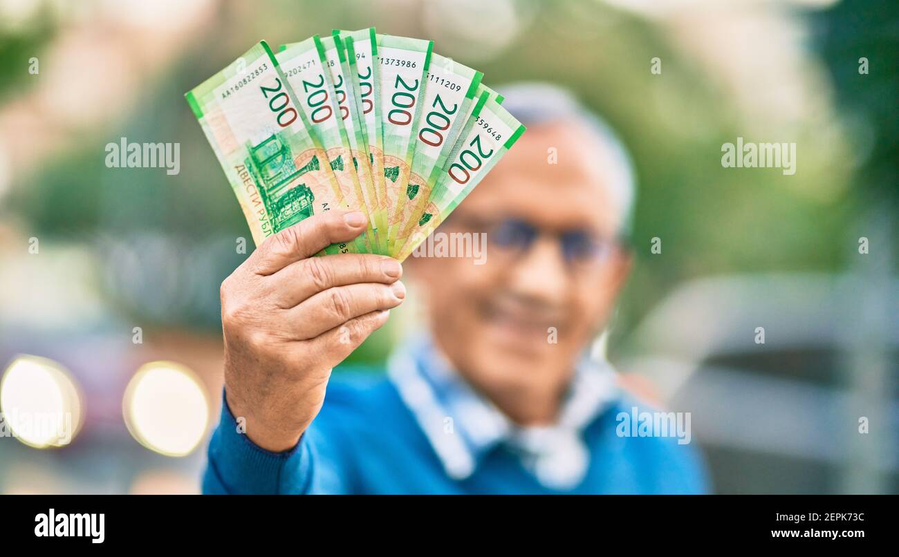 Senior grey-haired man smiling happy holding russian ruble banknotes at ...