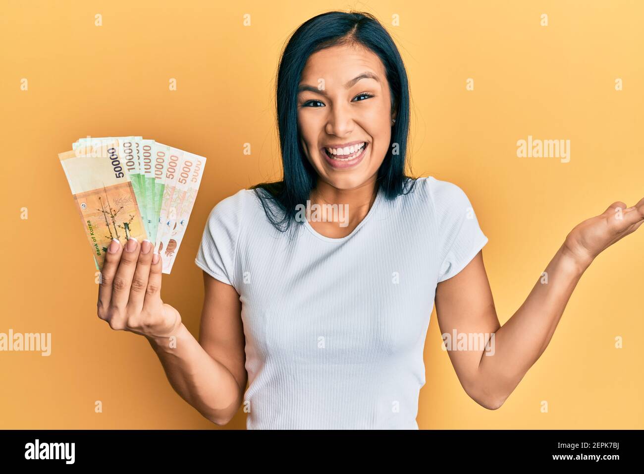 Beautiful hispanic woman holding south korean won banknotes celebrating ...