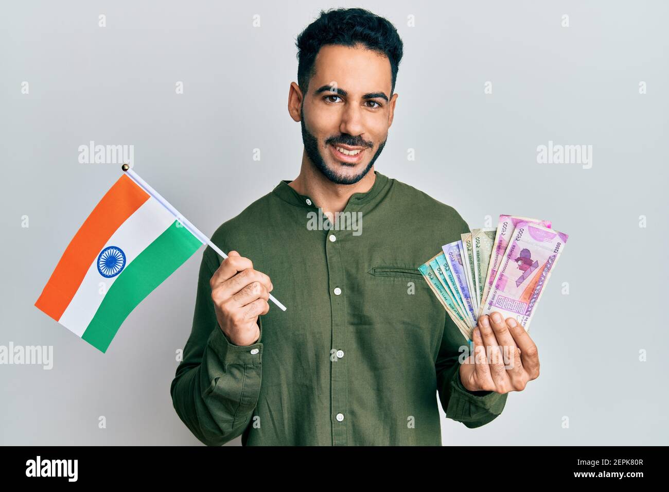 Young hispanic man holding india flag and rupee banknotes smiling with ...