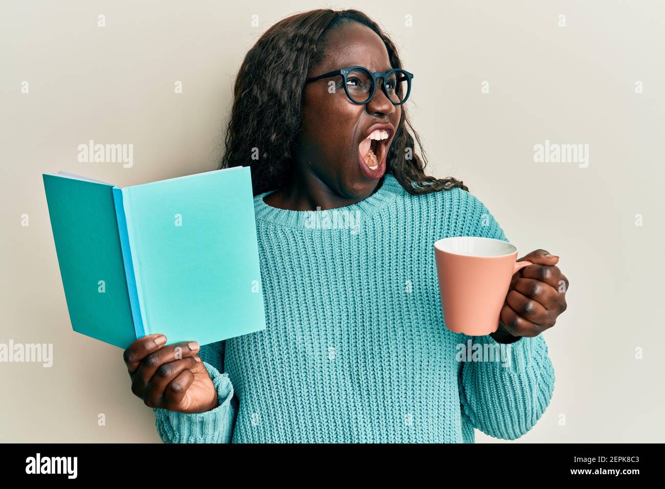 African young woman reading a book and drinking a cup of coffee angry ...