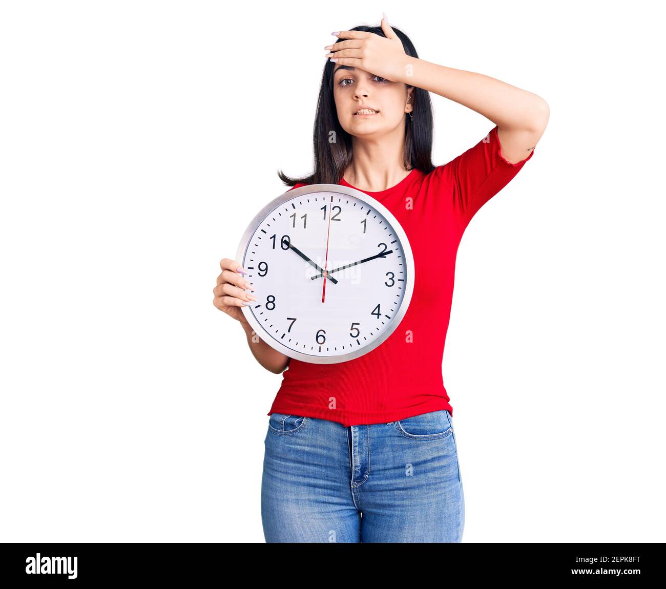 Young beautiful girl holding clock stressed and frustrated with hand on ...