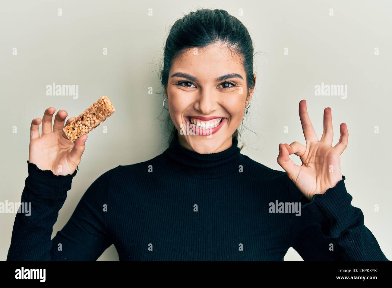 Young hispanic woman eating protein bar as healthy energy snack doing ...