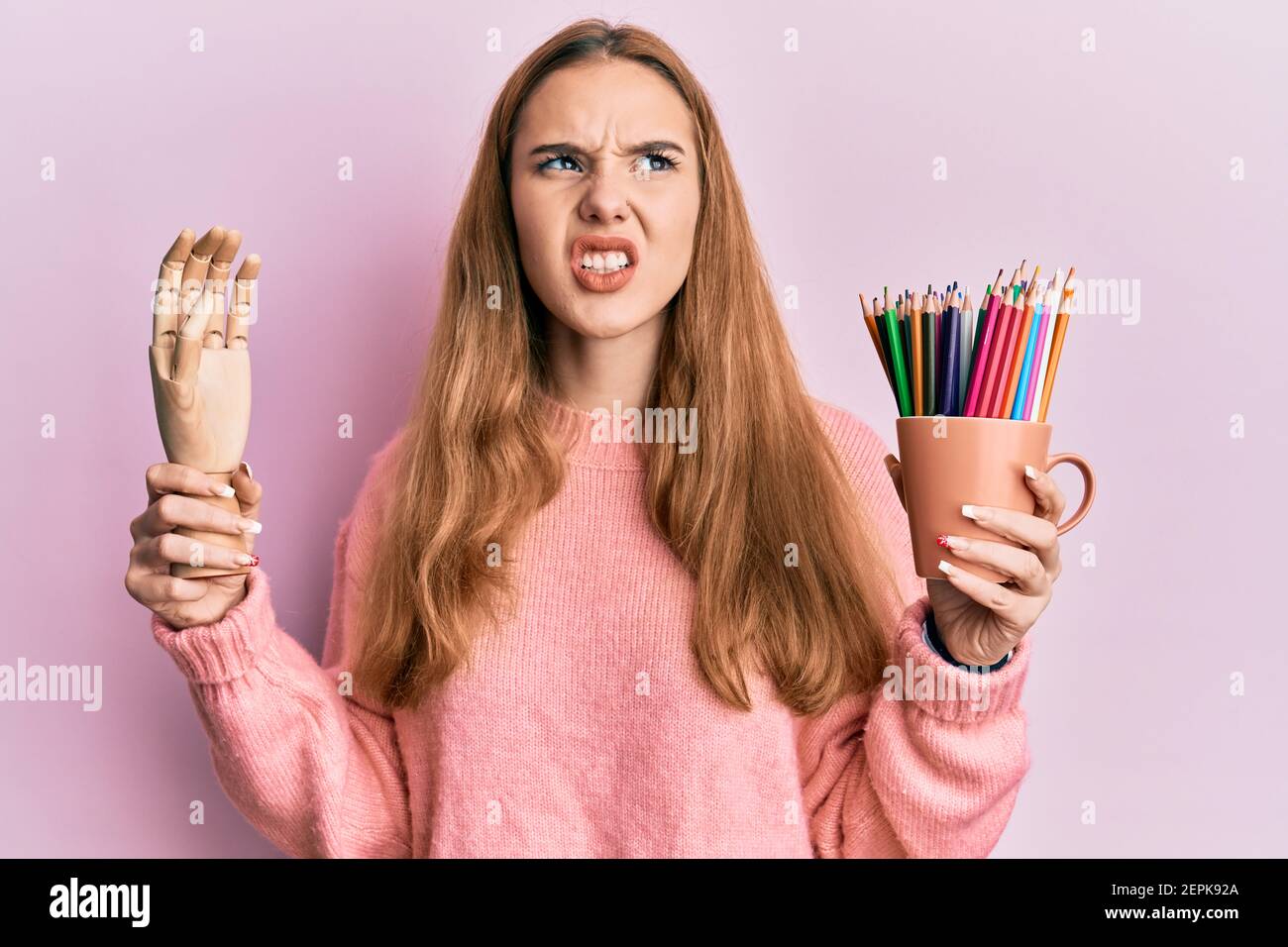 Young blonde woman holding small wooden manikin hand and pencils angry ...