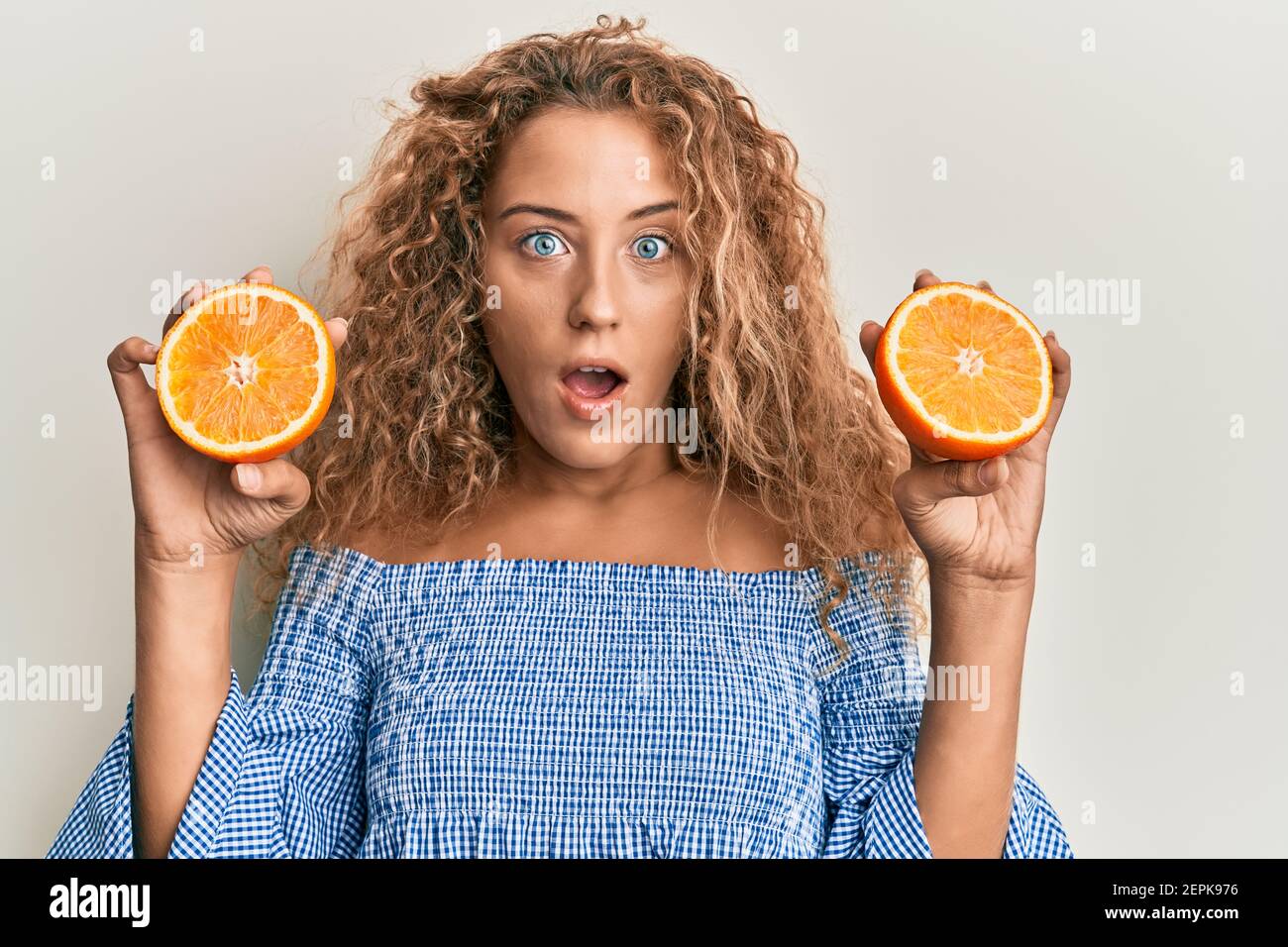 Beautiful caucasian teenager girl holding fresh orange afraid and ...