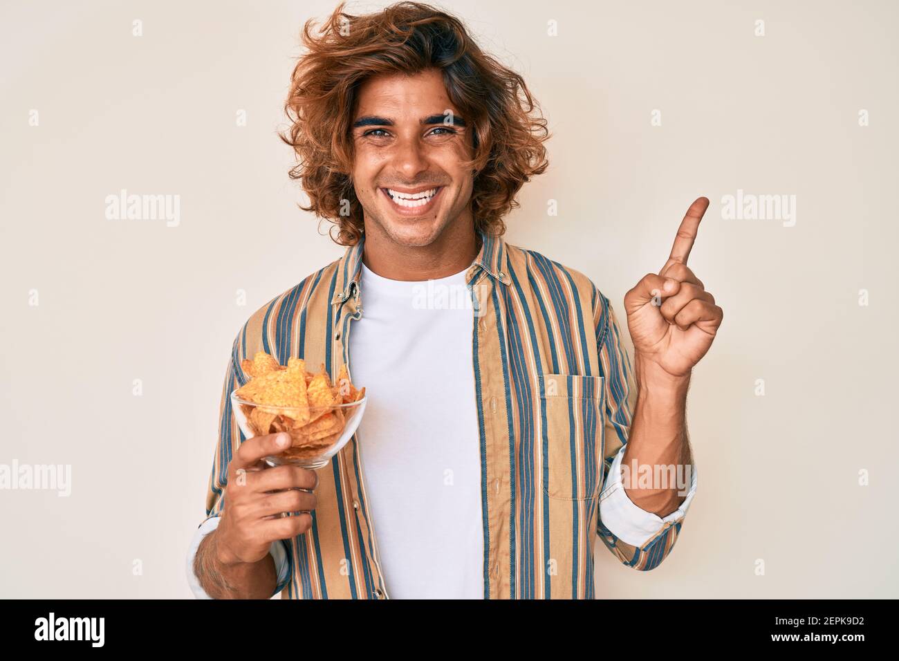 Young hispanic man holding nachos potato chips smiling happy pointing ...