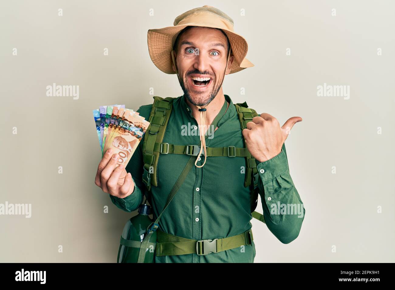 Handsome man with beard wearing explorer hat holding canadian dollars ...