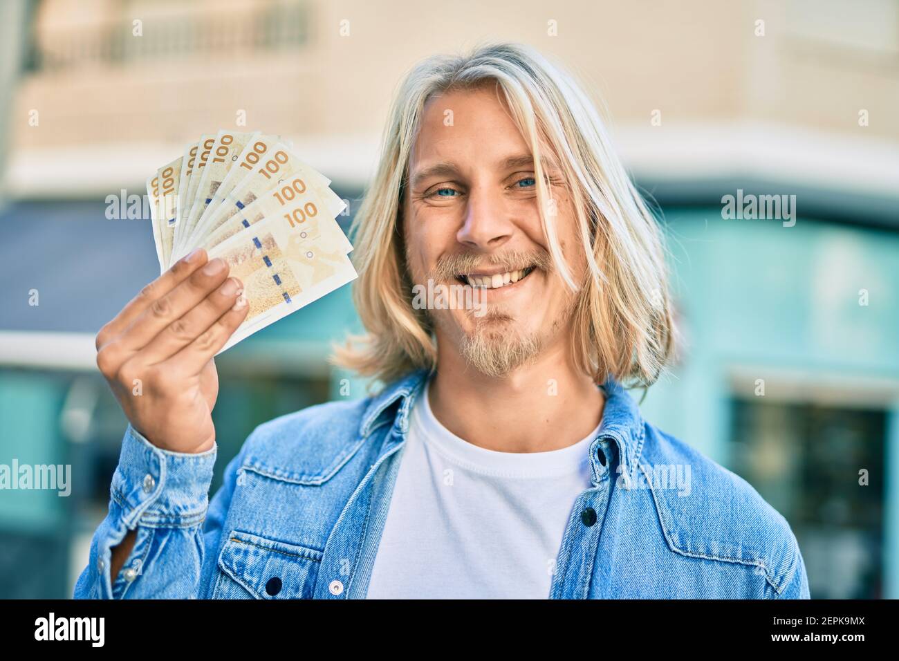 Young blond scandinavian man smiling happy holding danmark 100 kroner ...