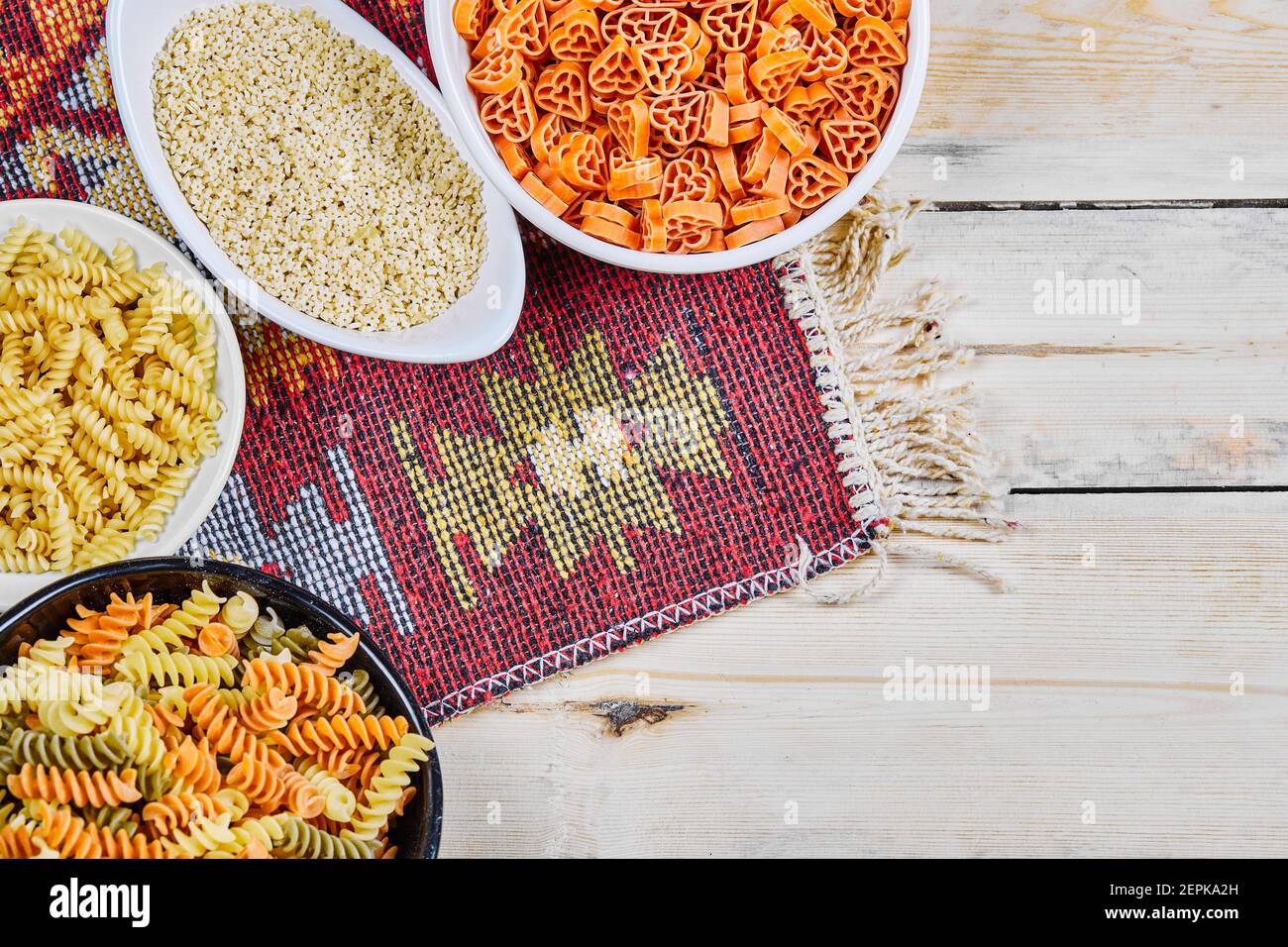 A bunch of colorful uncooked pasta bowls on wooden table with carved ...