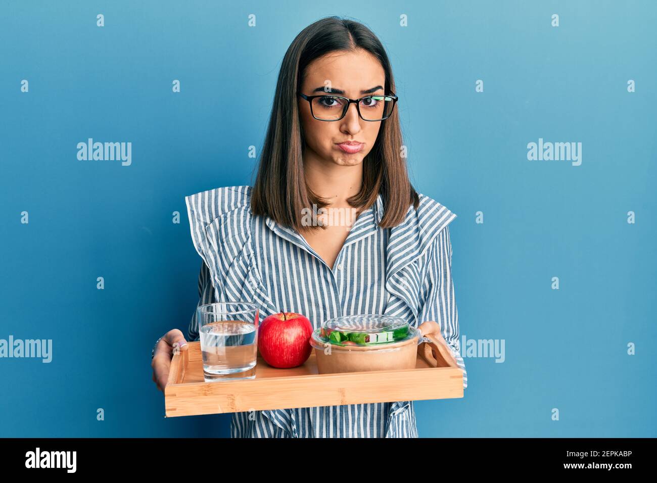 Young brunette girl holding tray with healthy lunch depressed and worry ...