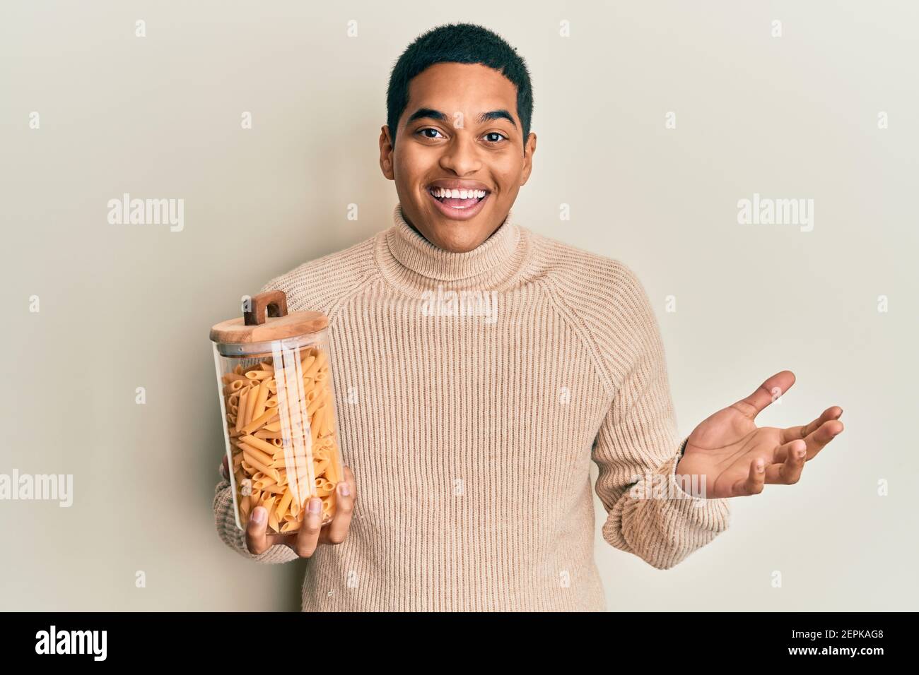 Young handsome hispanic man holding jar with macaroni pasta celebrating ...