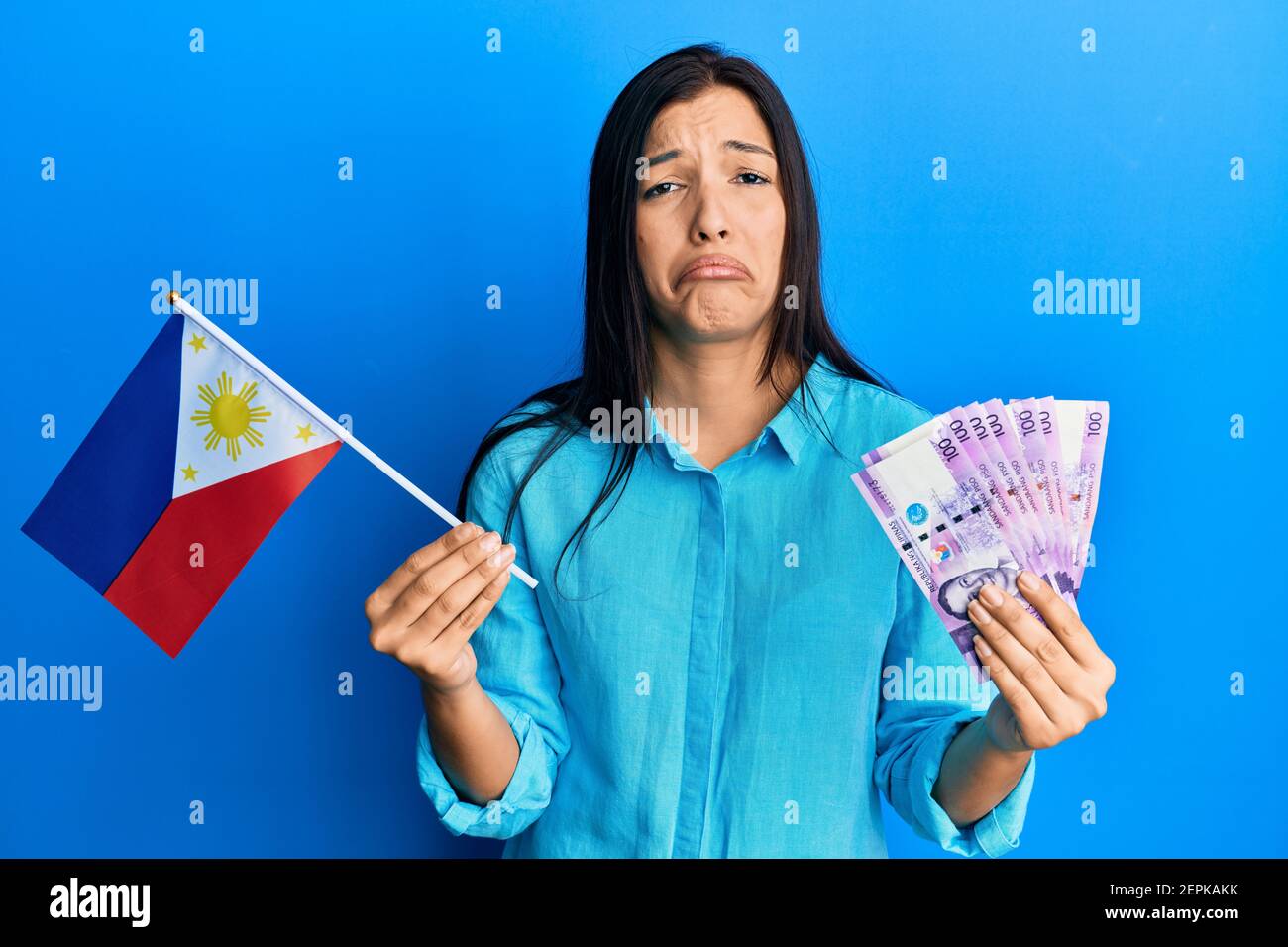 Young latin woman holding philippines flag and pesos banknotes ...