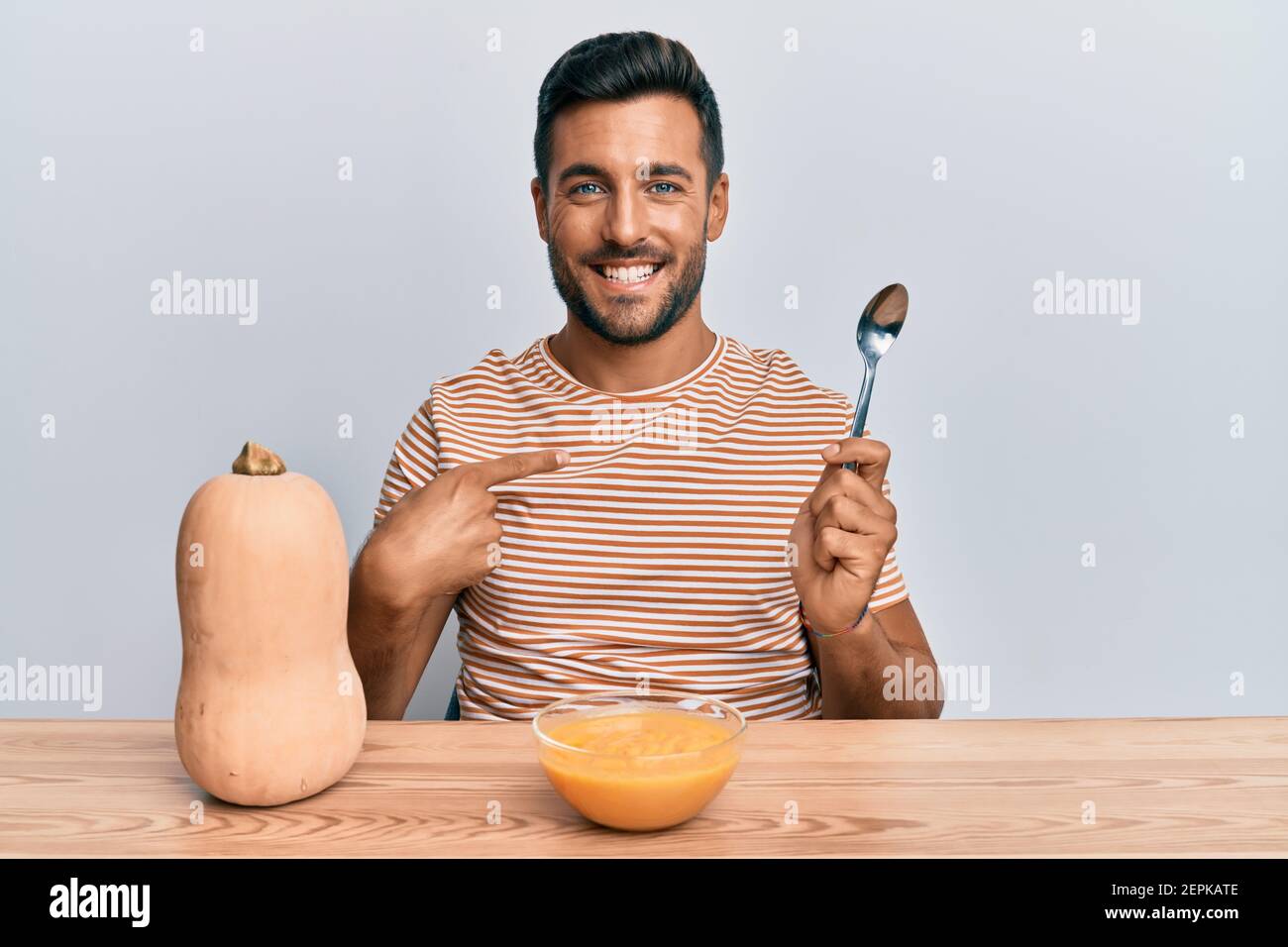 Handsome hispanic man eating pumpkin soup with spoon pointing finger to ...
