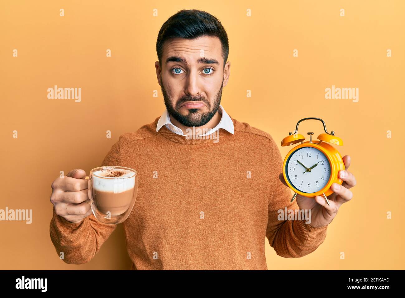 Young hispanic man holding coffee and alarm clock depressed and worry ...
