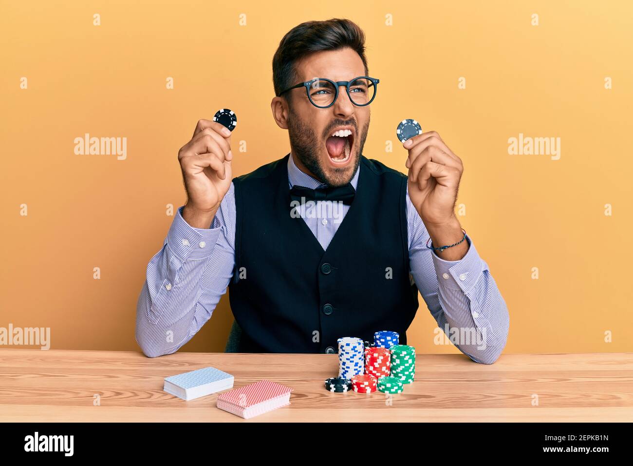 Handsome hispanic croupier man sitting on the table holding casino ...