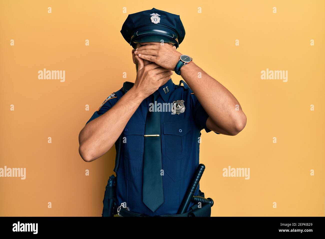 Handsome hispanic man wearing police uniform covering eyes and mouth ...