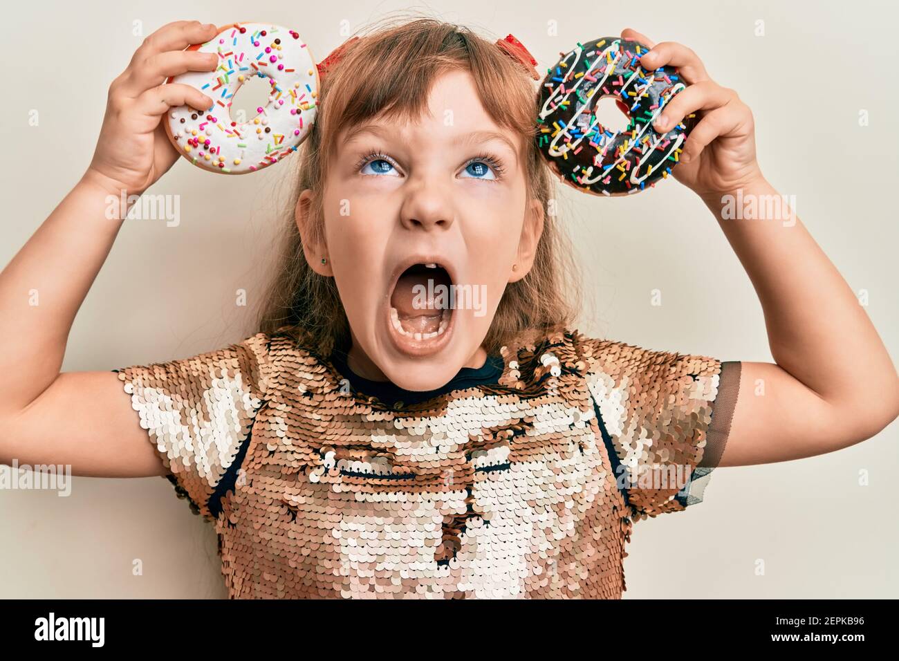 Little caucasian girl kid holding tasty colorful doughnuts angry and ...