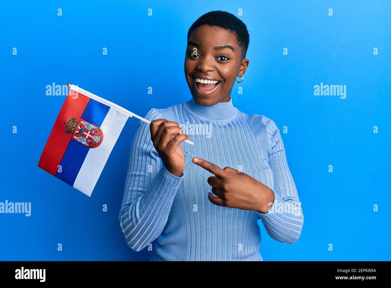 Young african american woman holding serbia flag smiling happy pointing ...