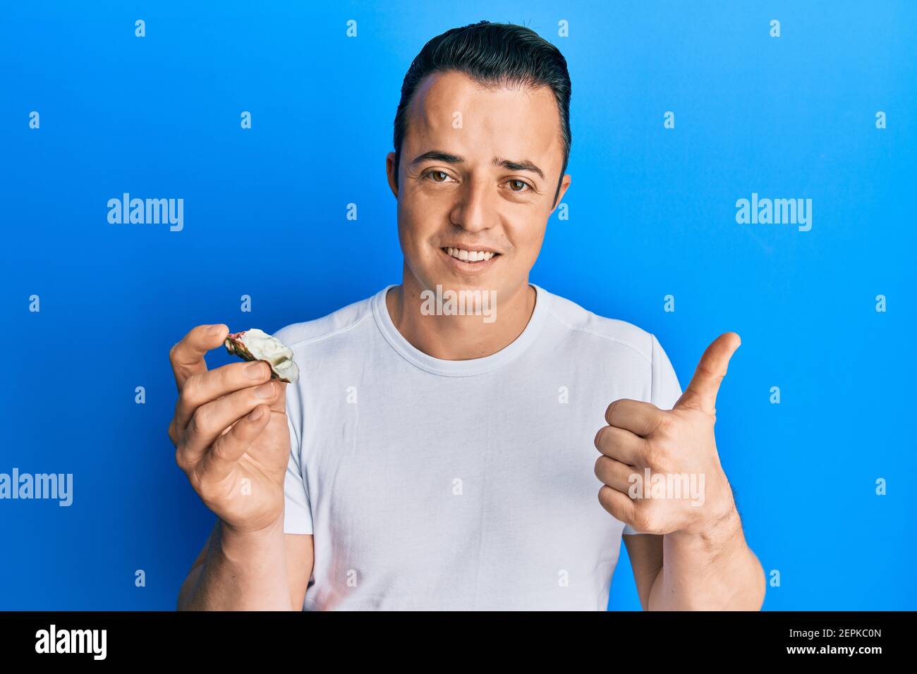 Handsome young man holding raw oyster smiling happy and positive, thumb ...