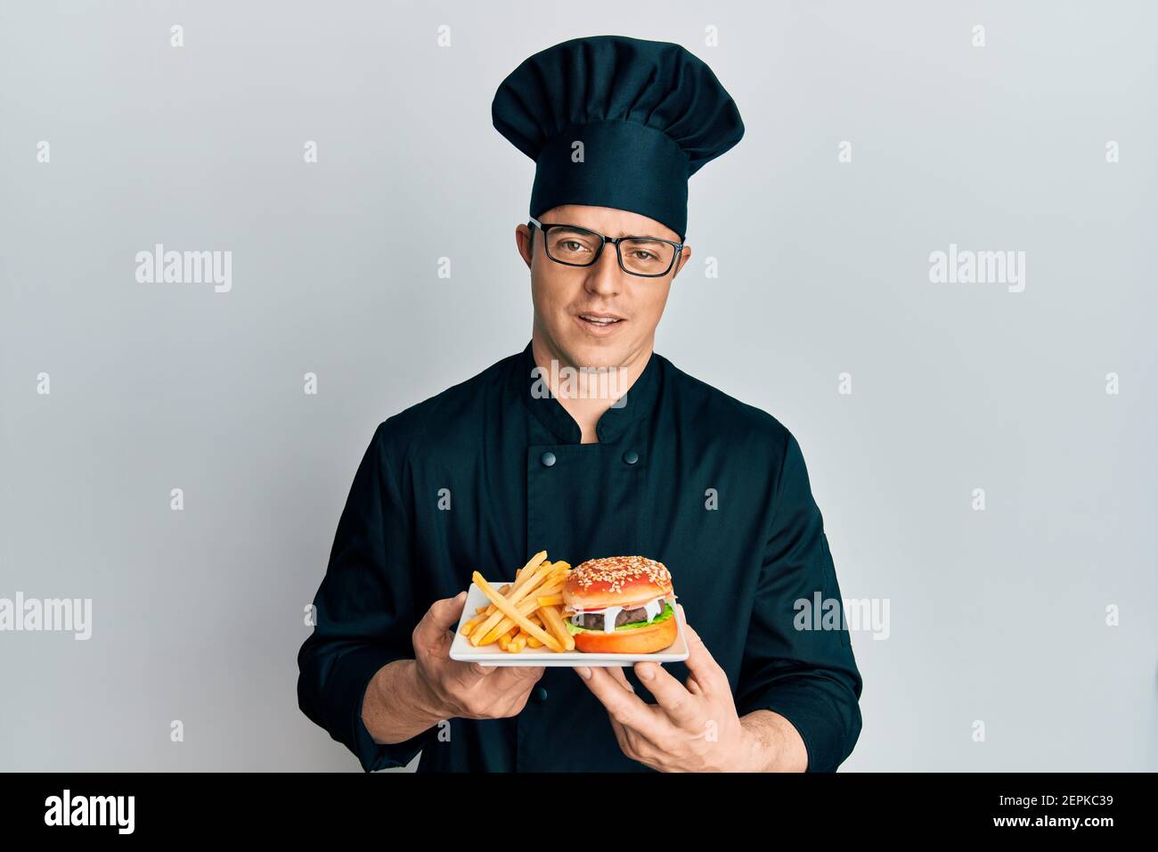 Handsome young man chef holding burger with fries in shock face ...