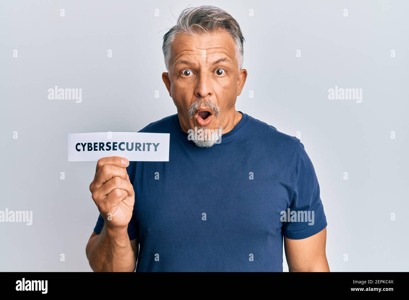 Middle Age Grey Haired Man Holding Cybersecurity Word Paper Scared And Amazed With Open Mouth