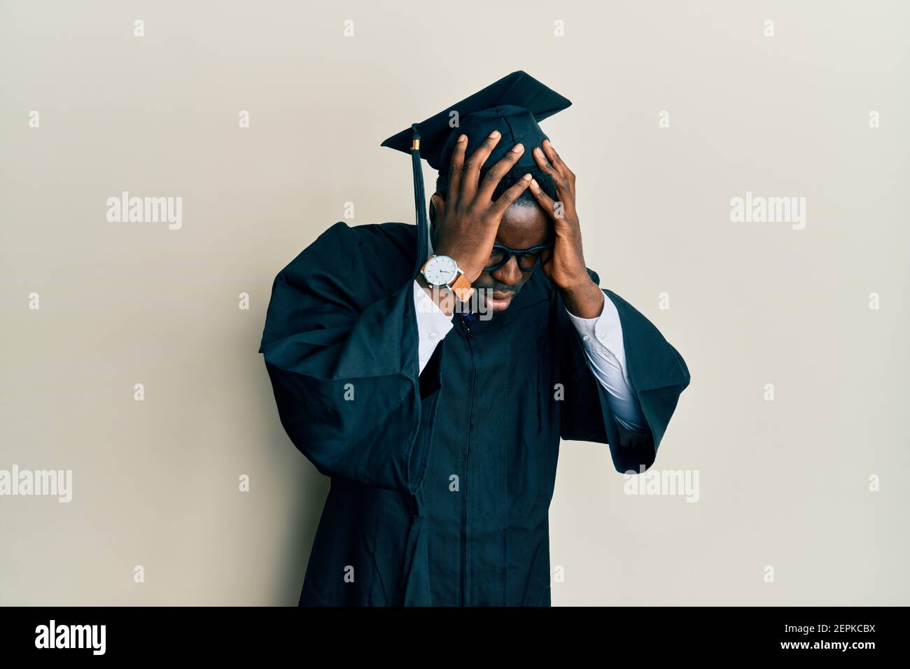 Handsome black man wearing graduation cap and ceremony robe suffering ...