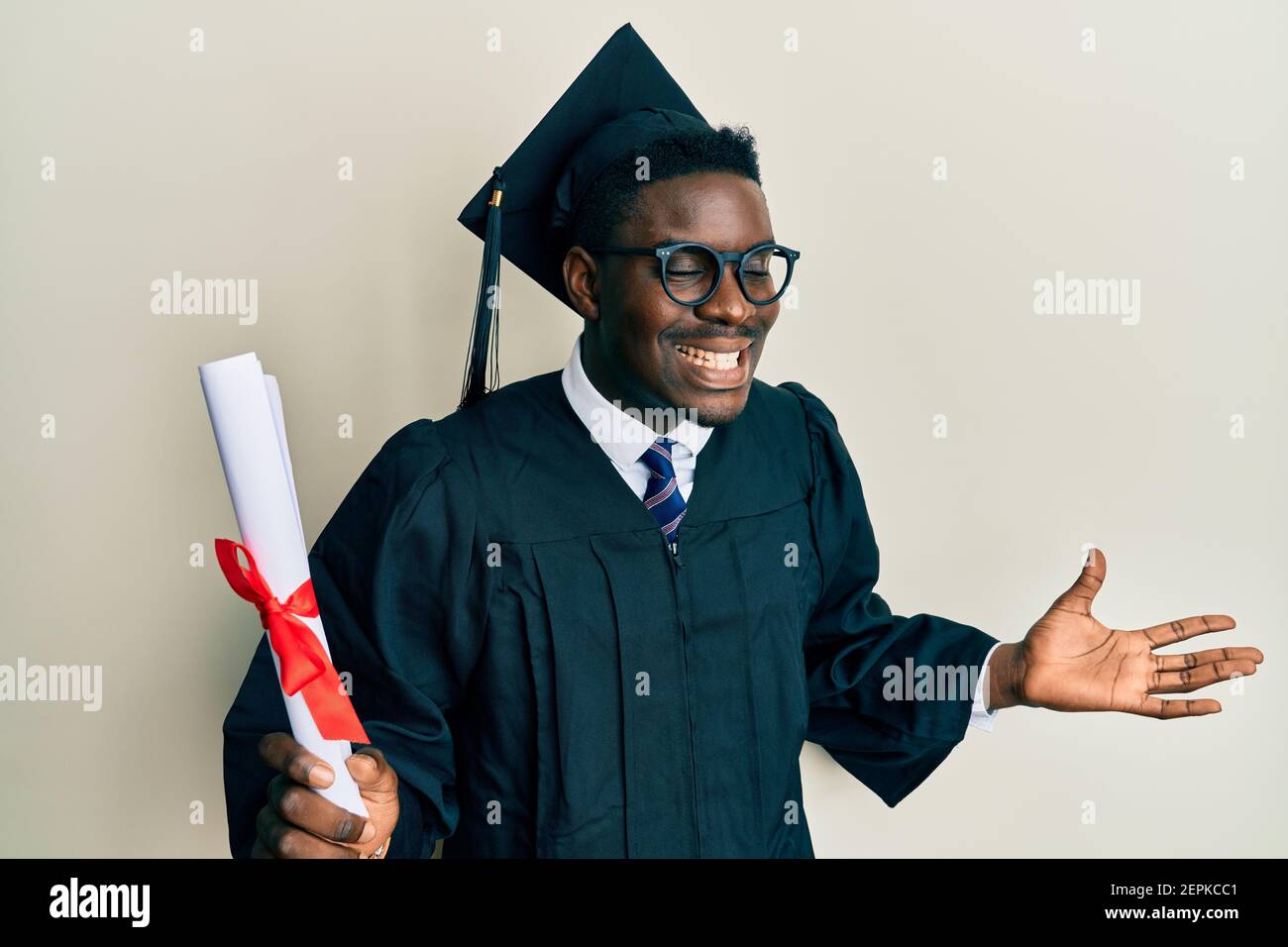 Handsome black man wearing graduation cap and ceremony robe holding ...