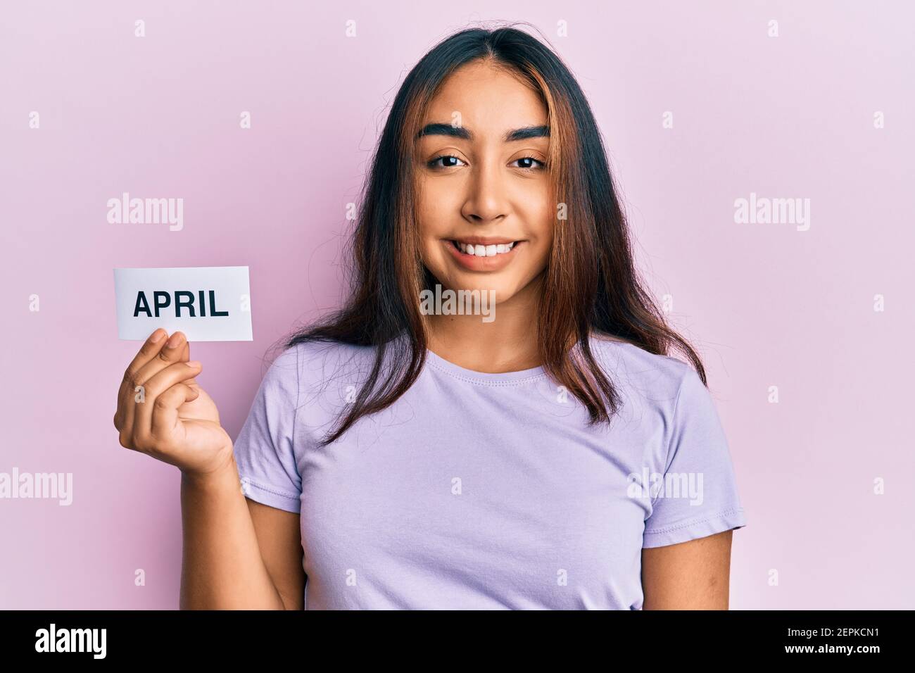 Young latin woman holding april word paper looking positive and happy ...
