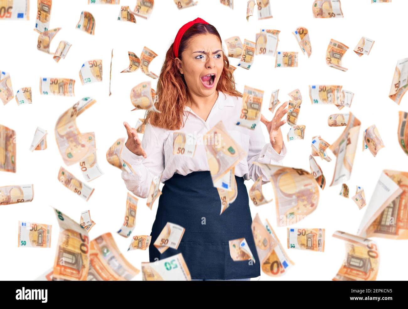 Young latin woman wearing waitress apron crazy and mad shouting and ...