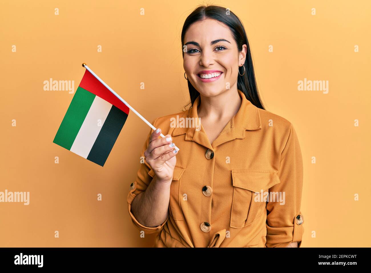 Young brunette woman holding united arab emirates flag looking positive ...