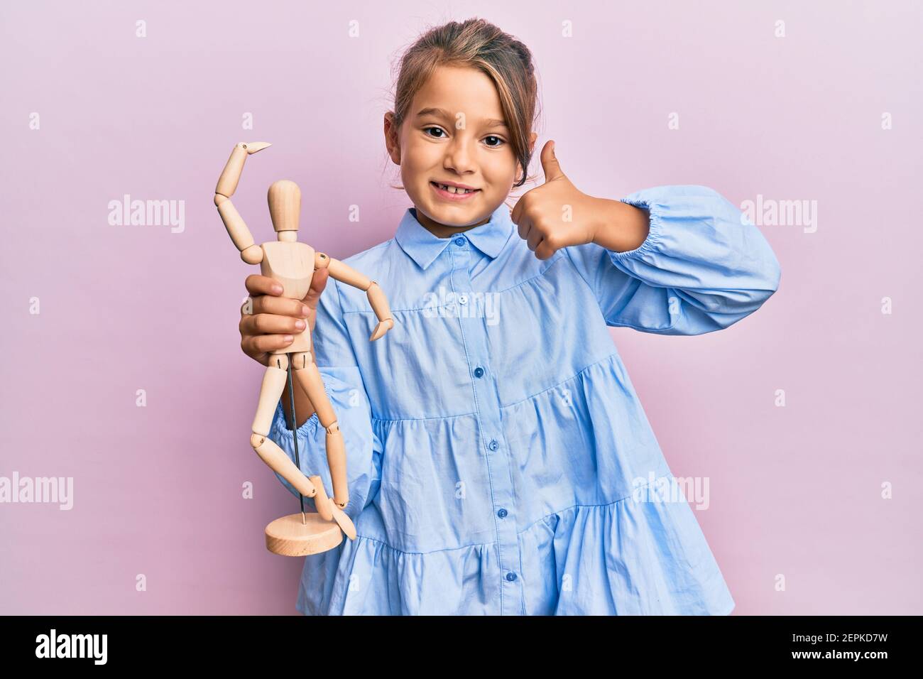 Little beautiful girl holding small wooden manikin smiling happy and ...