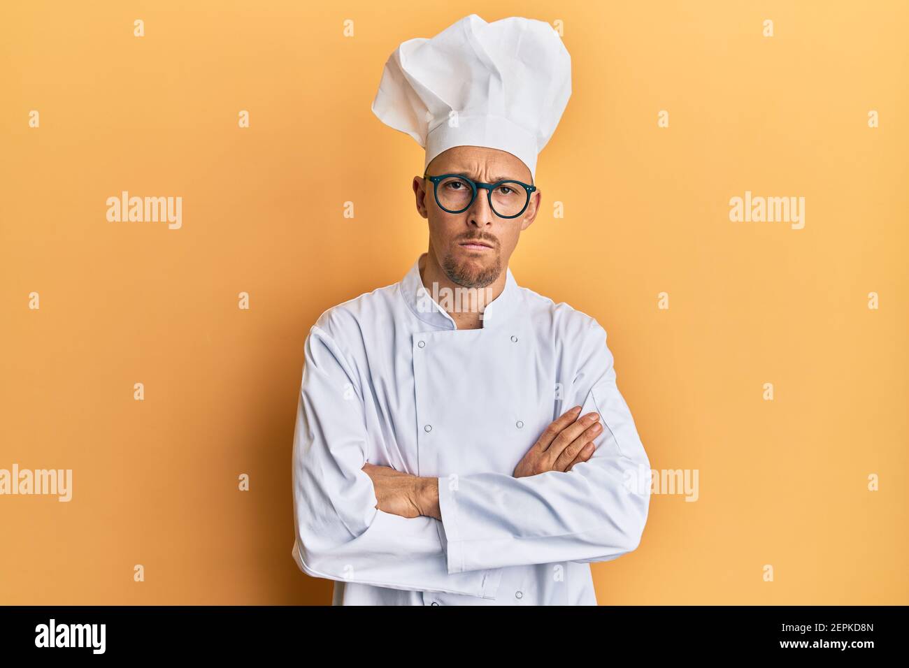 Bald man with beard wearing professional cook uniform skeptic and ...