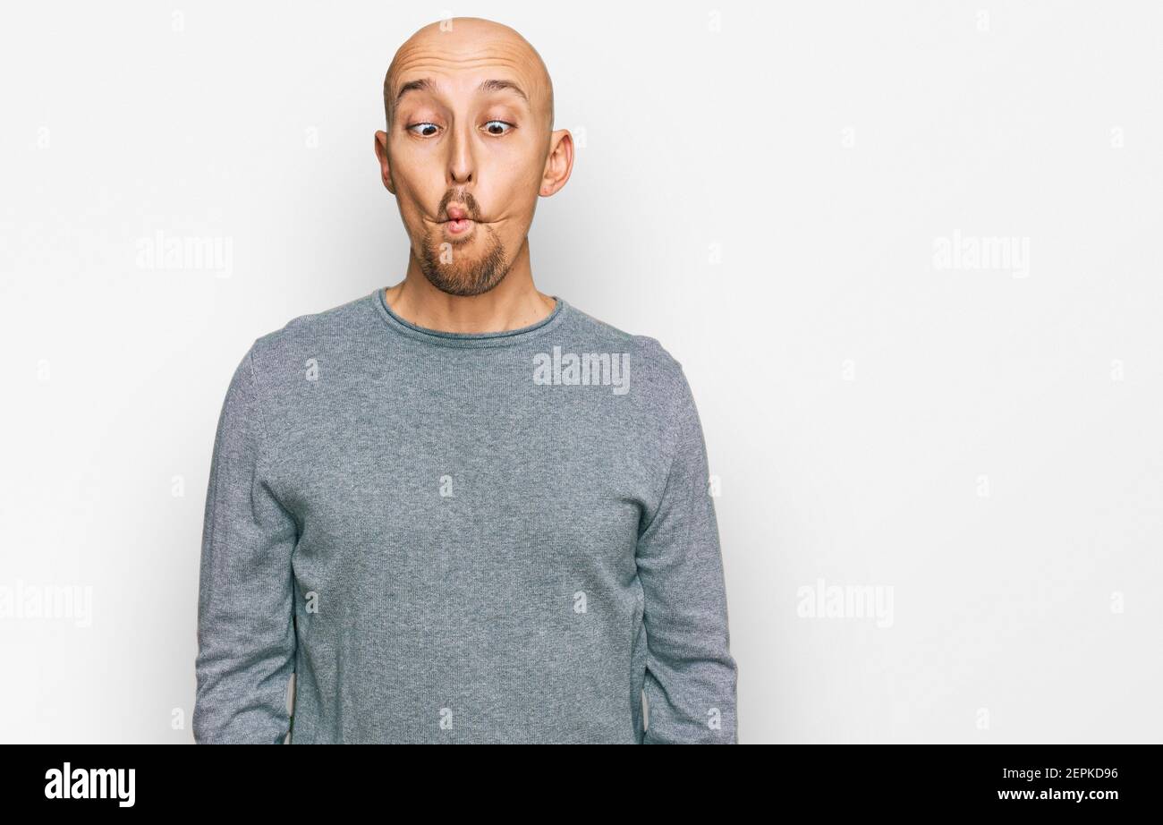 Bald man with beard wearing casual clothes making fish face with lips ...