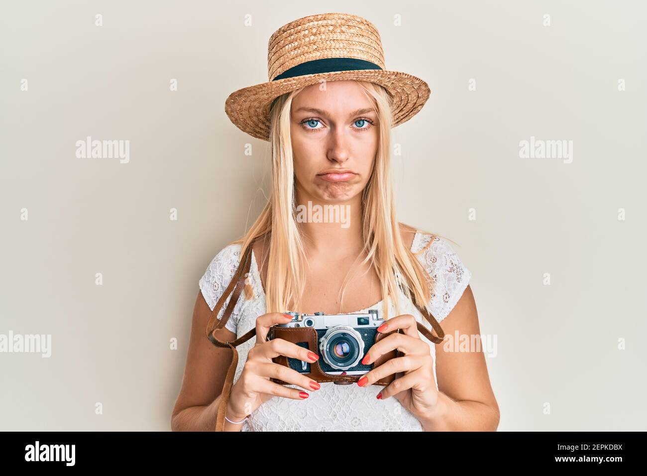 Young blonde girl wearing summer hat using camera depressed and worry ...