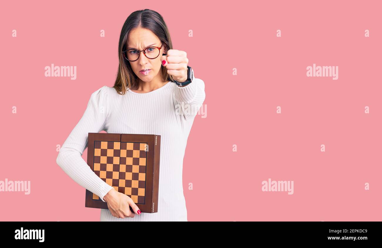 Beautiful brunette young woman holding chess annoyed and frustrated ...