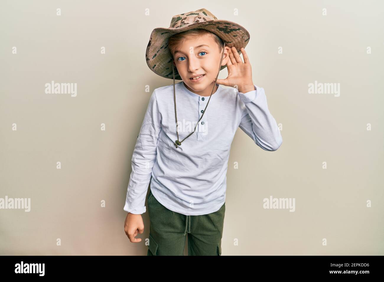 Little caucasian boy kid wearing explorer hat smiling with hand over ...