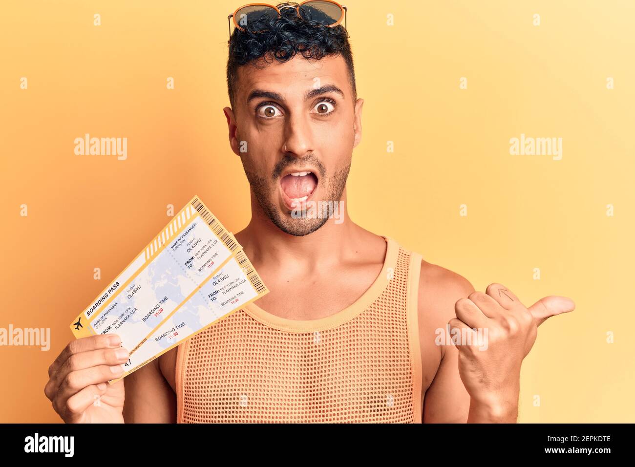 Young hispanic man holding boarding pass pointing thumb up to the side ...