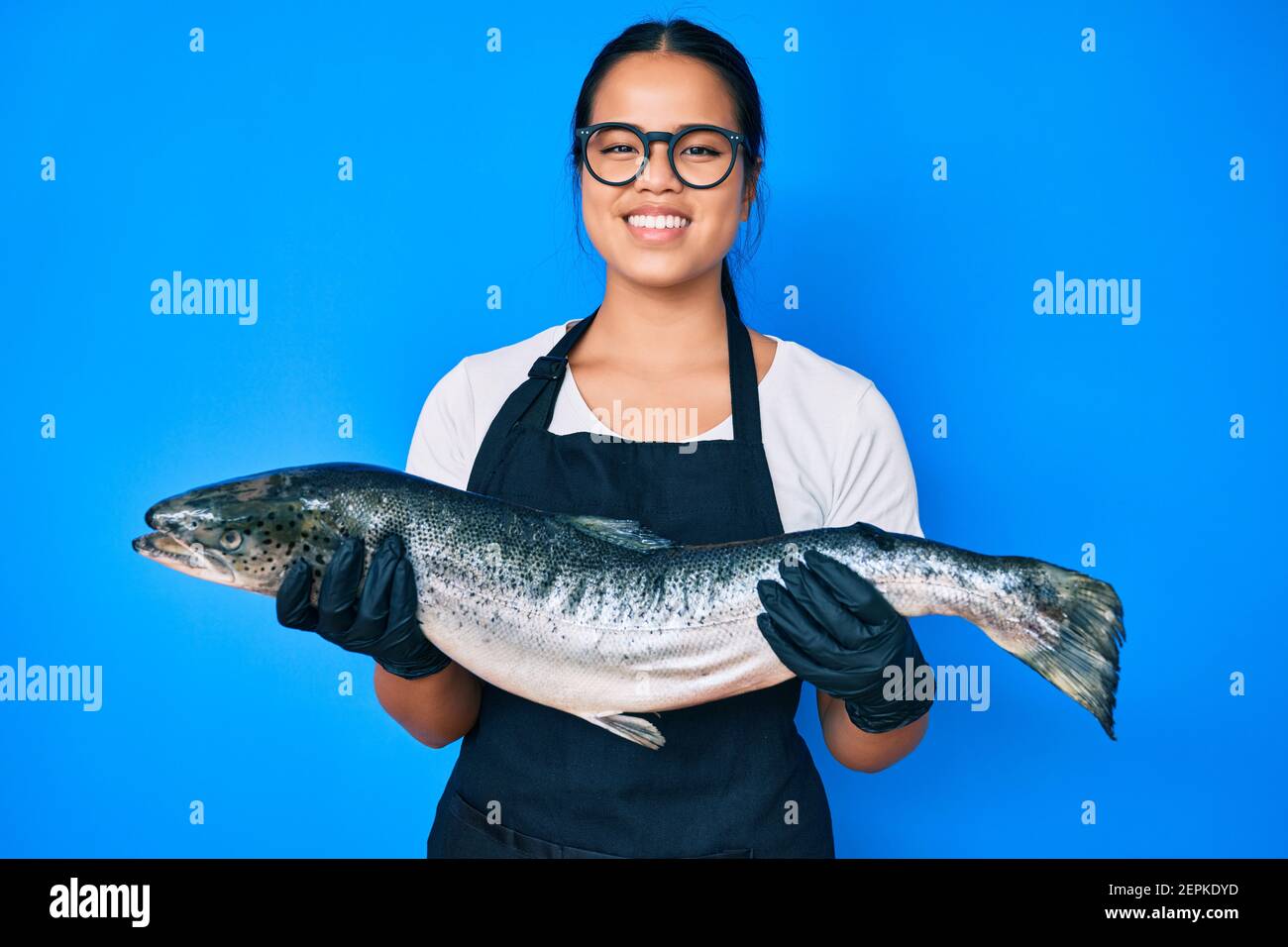 Young beautiful asian girl fishmonger selling fresh raw salmon smiling ...