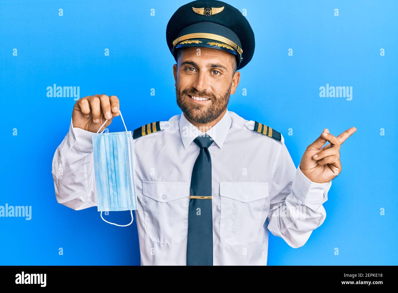 Handsome man with beard wearing airplane pilot uniform holding safety ...