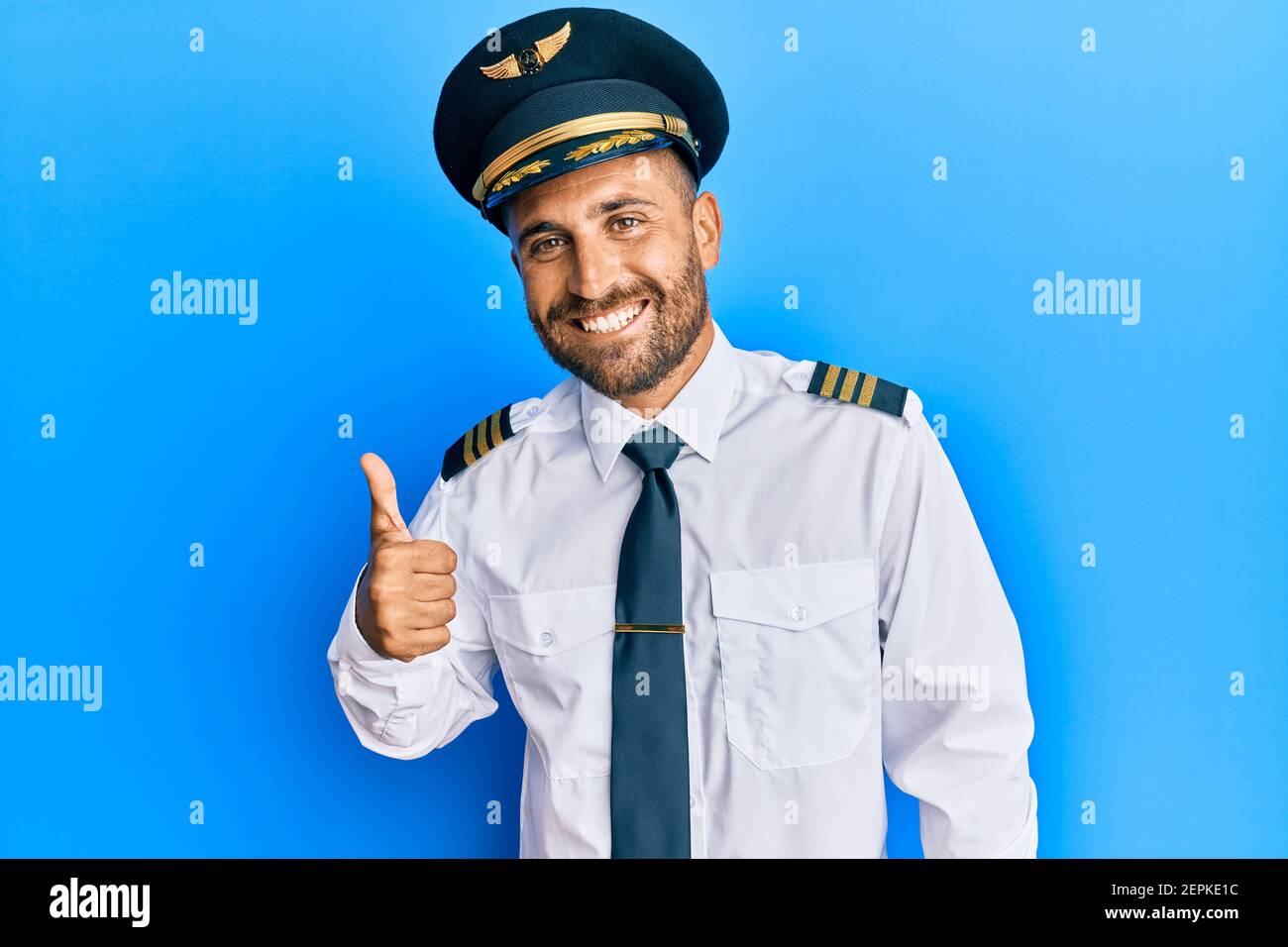 Handsome man with beard wearing airplane pilot uniform doing happy ...
