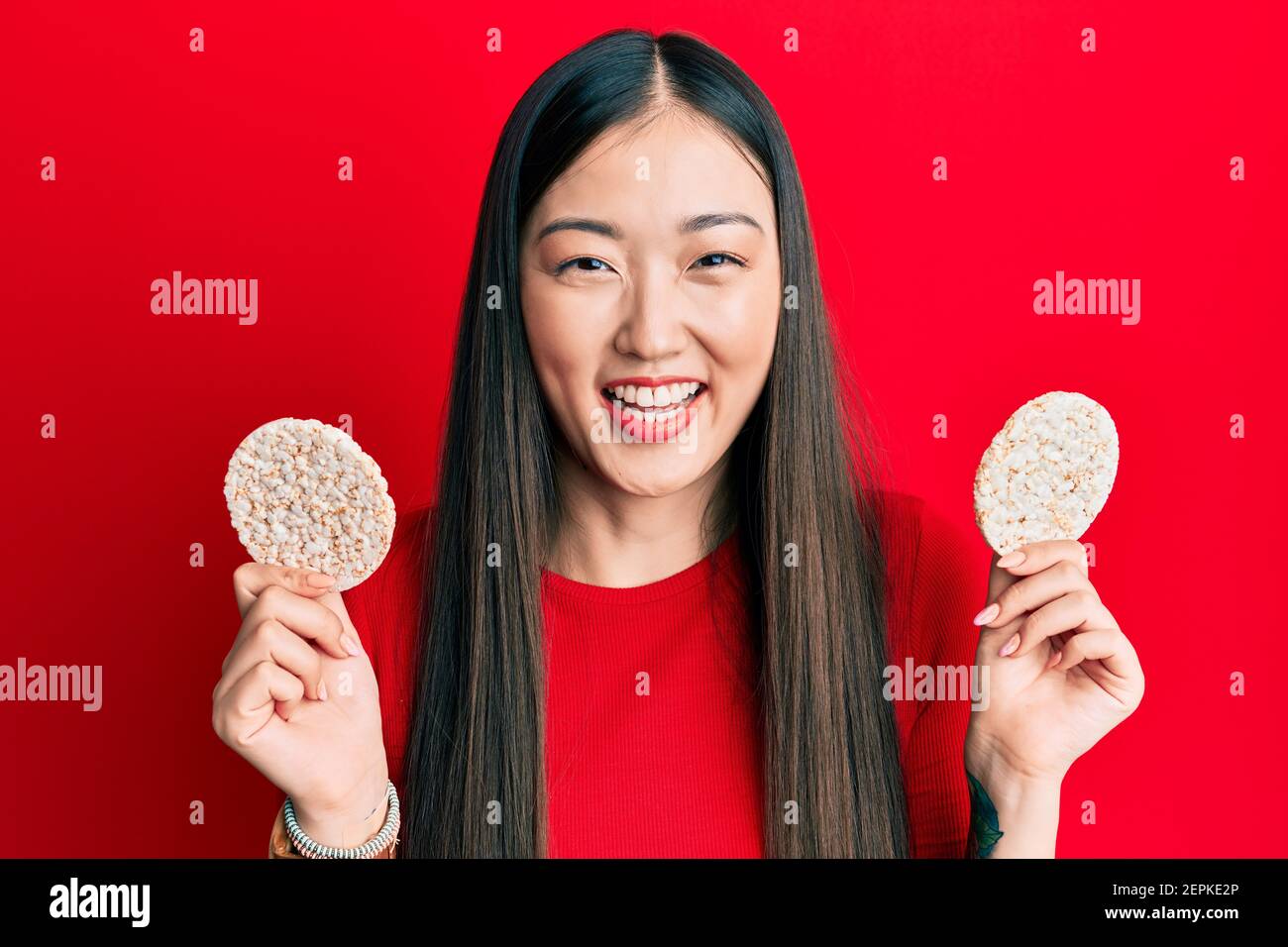 Young chinese woman eating healthy rice crackers smiling and laughing ...