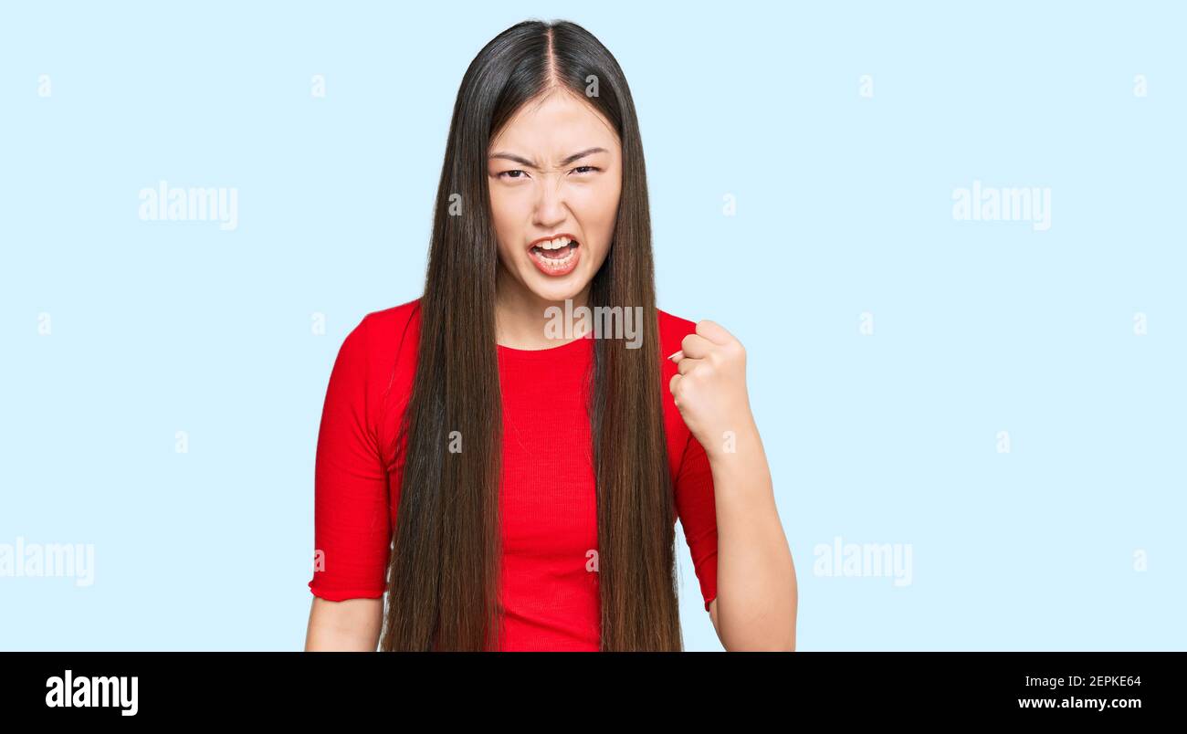 Young chinese woman wearing casual clothes angry and mad raising fist ...