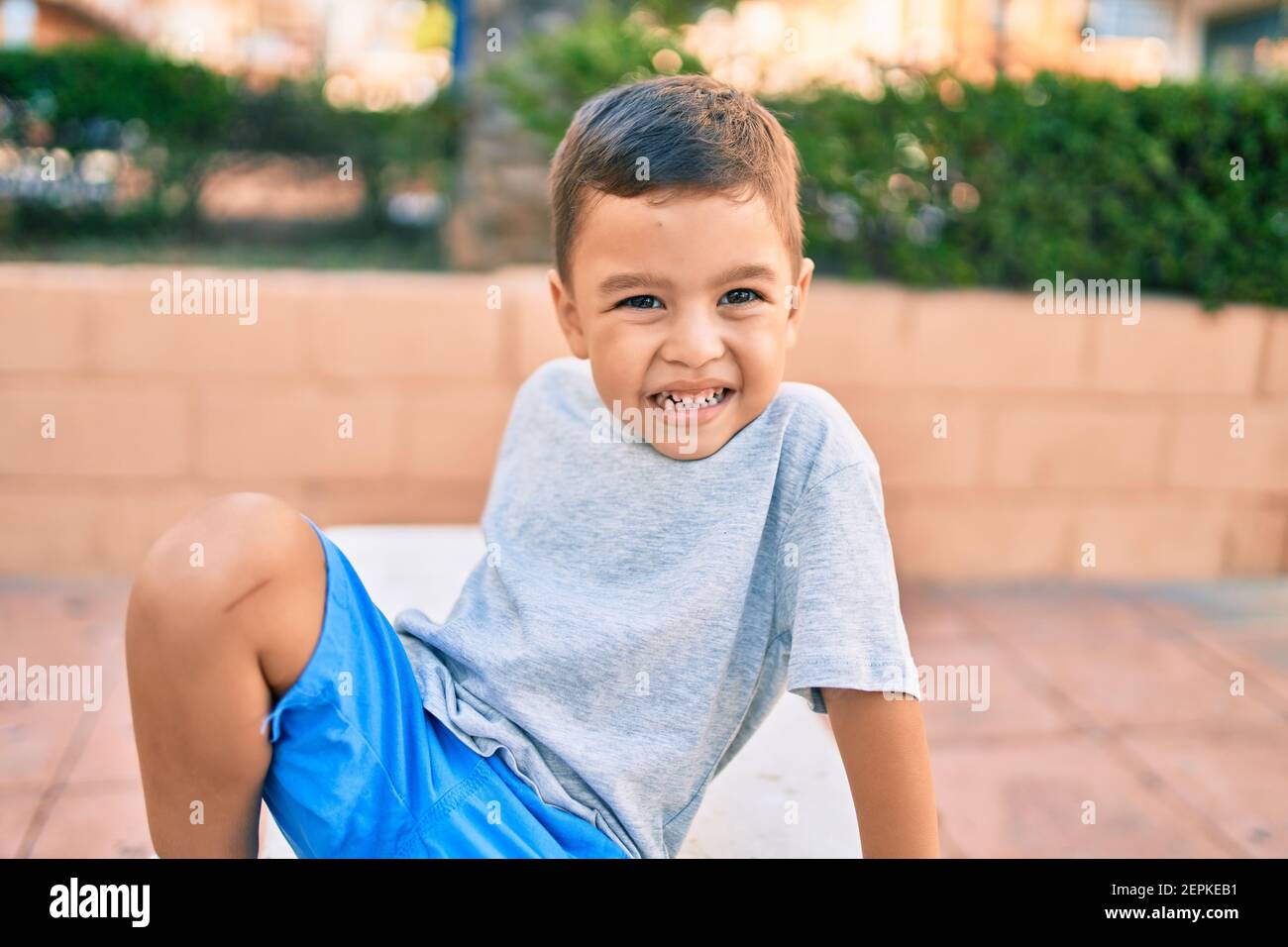 Adorable hispanic boy smiling happy sitting on the bench at the park ...